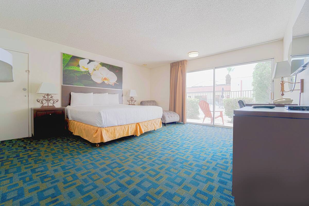 Quarto de hotel com uma cama grande, uma mesa com luminária, uma cadeira e vista para o exterior.