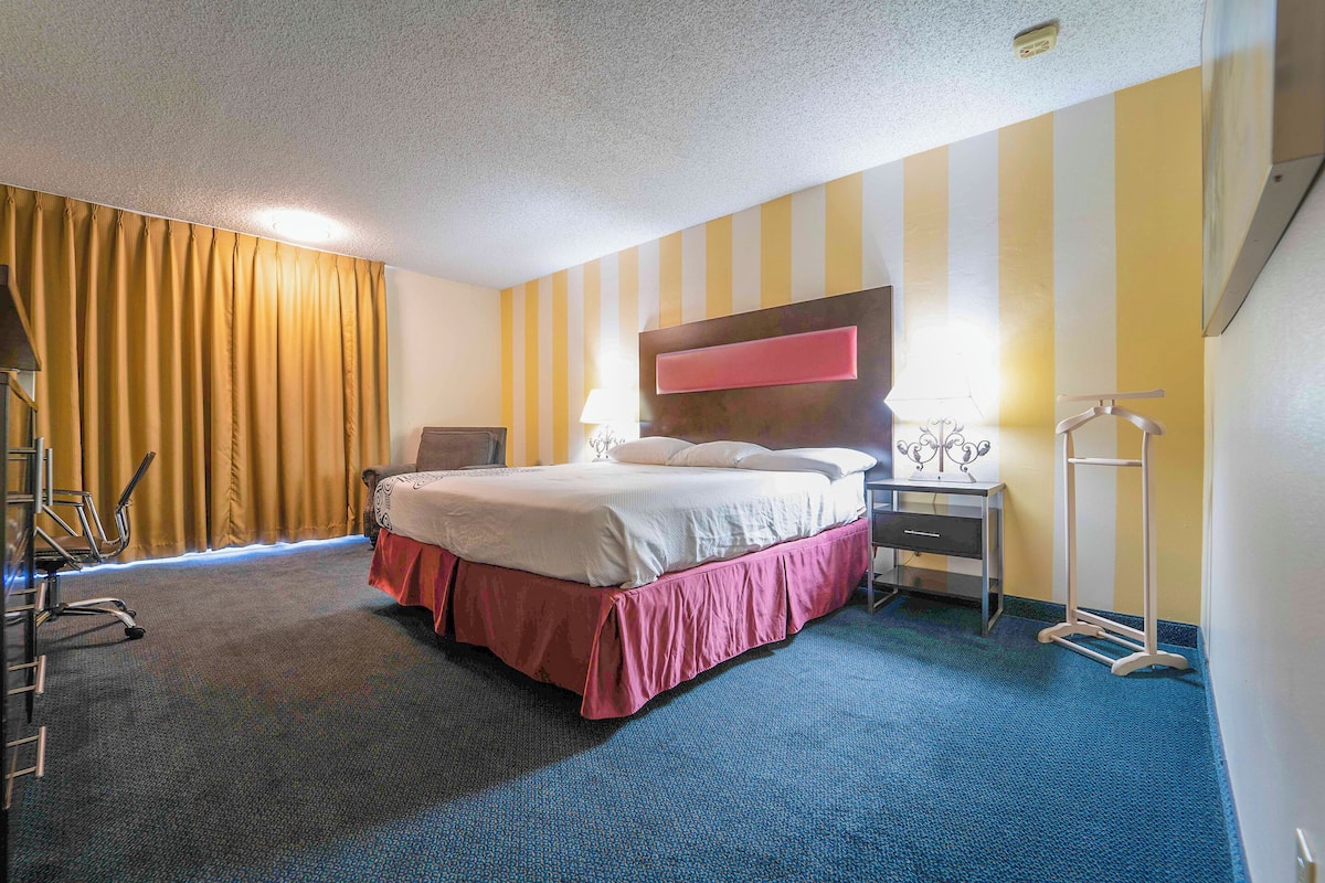 Quarto de hotel com cama, escrivaninha, cadeira, abajur e guarda-roupa.