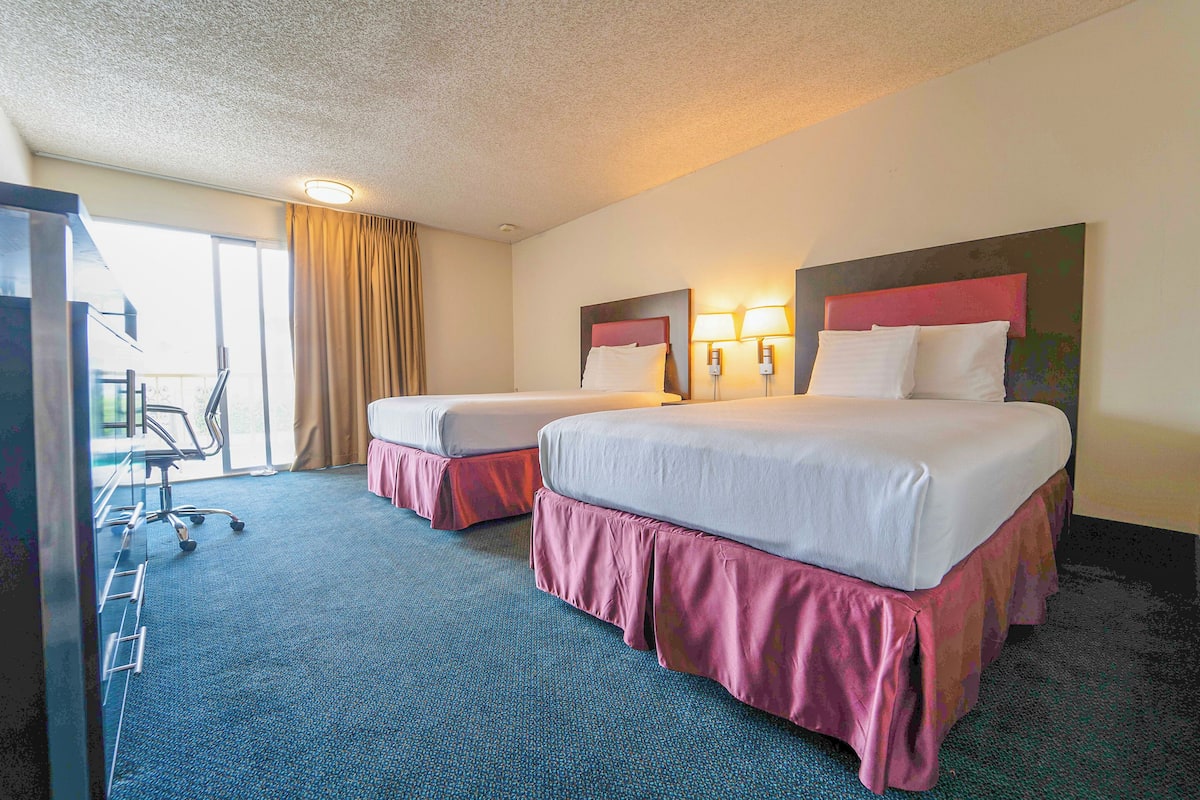 Quarto de hotel com duas camas, uma escrivaninha e uma cadeira.