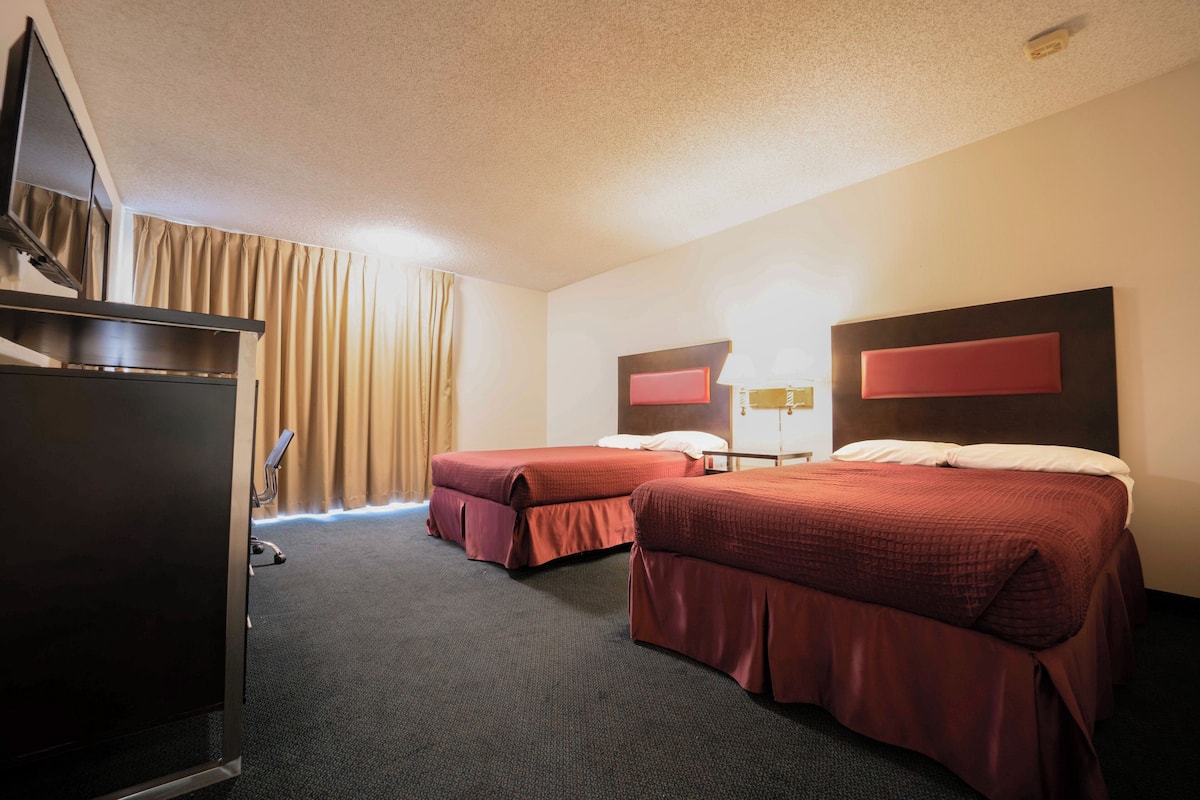 Quarto de hotel com duas camas, uma escrivaninha e uma televisão.