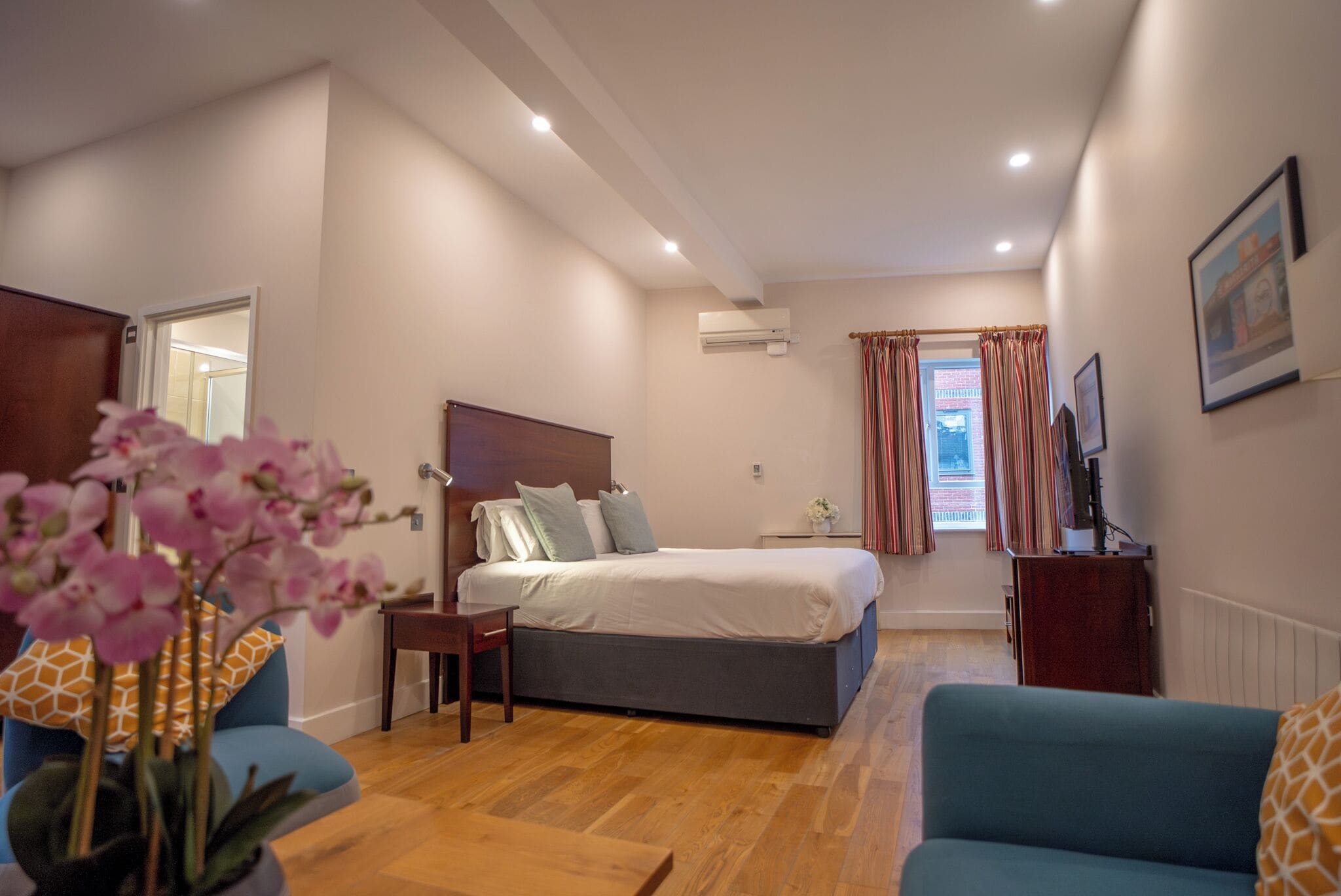 Quarto com cama, escrivaninha, cadeira, televisão e janela com cortinas.