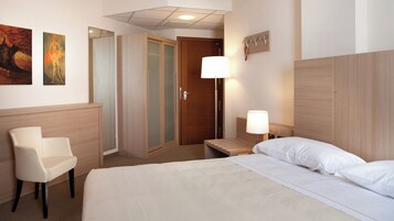Quarto de hotel com cama, poltrona, escrivaninha e luminária.