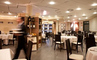 Restaurante com várias mesas, cadeiras e uma seleção de vinhos.