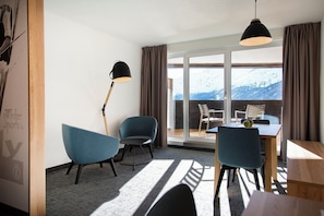 Quarto de hotel com varanda, duas cadeiras, uma mesa e um abajur.