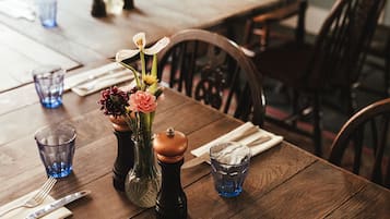 Uma mesa de jantar de madeira com um vaso de flores, saleiro e pimenteiro, e copos de vidro azul.