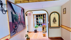 Corredor com cadeiras vermelhas, uma pintura grande, plantas em vasos e piso de azulejos.