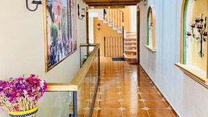 Um corredor com piso de azulejos, vigas de madeira, uma escadaria e um vaso de flores sobre uma mesa.