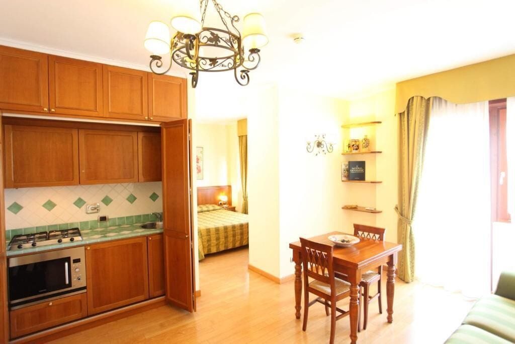Cozinha compacta com armários de madeira, fogão a gás e micro-ondas. Possui uma área de jantar com mesa e cadeiras de madeira.