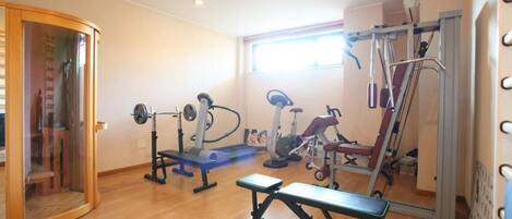 Uma academia em casa com equipamentos de exercício, uma porta de correr de vidro e piso de madeira.