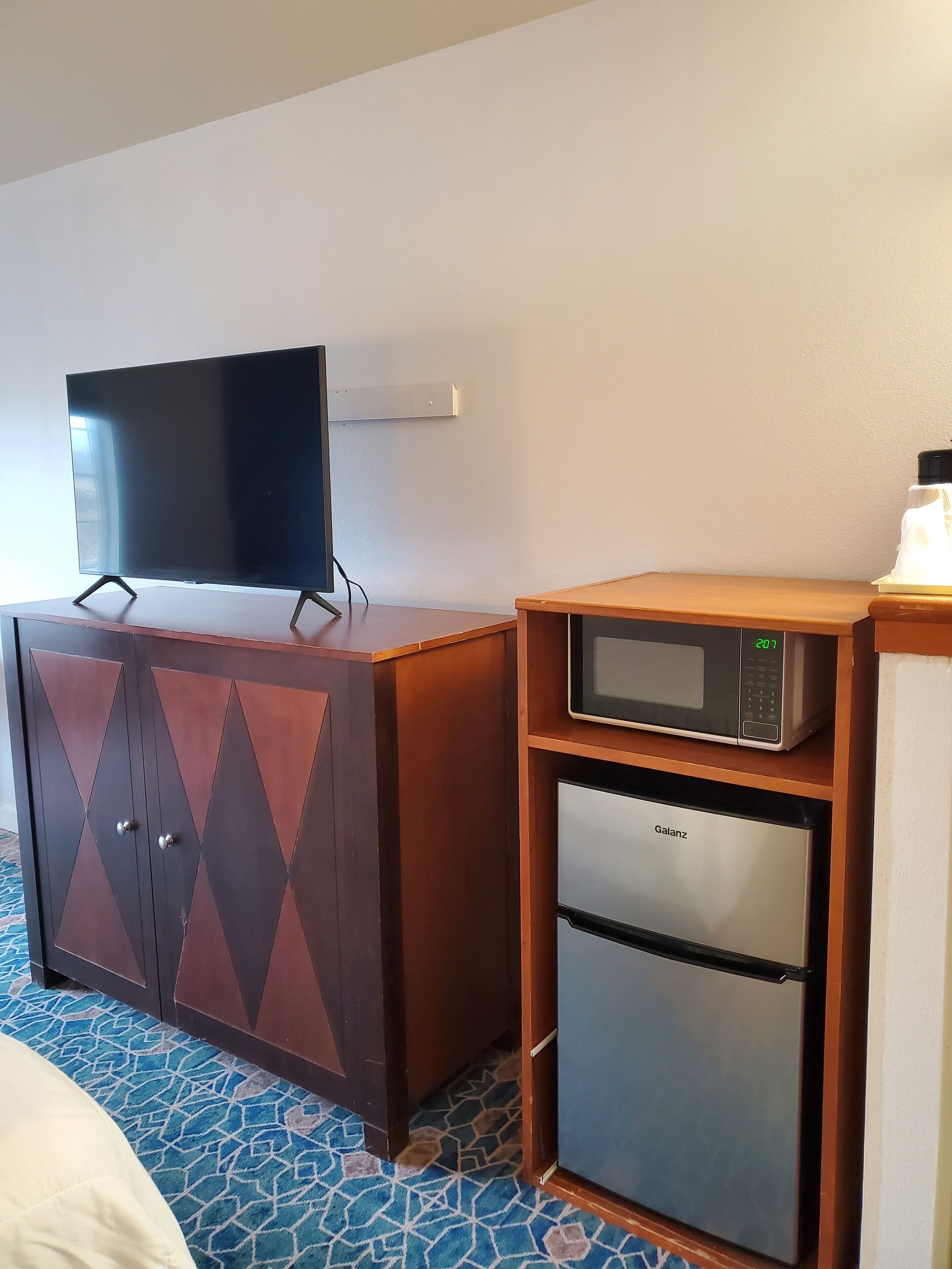 Quarto de hotel com televisão sobre um armário de madeira, micro-ondas e frigorífico.