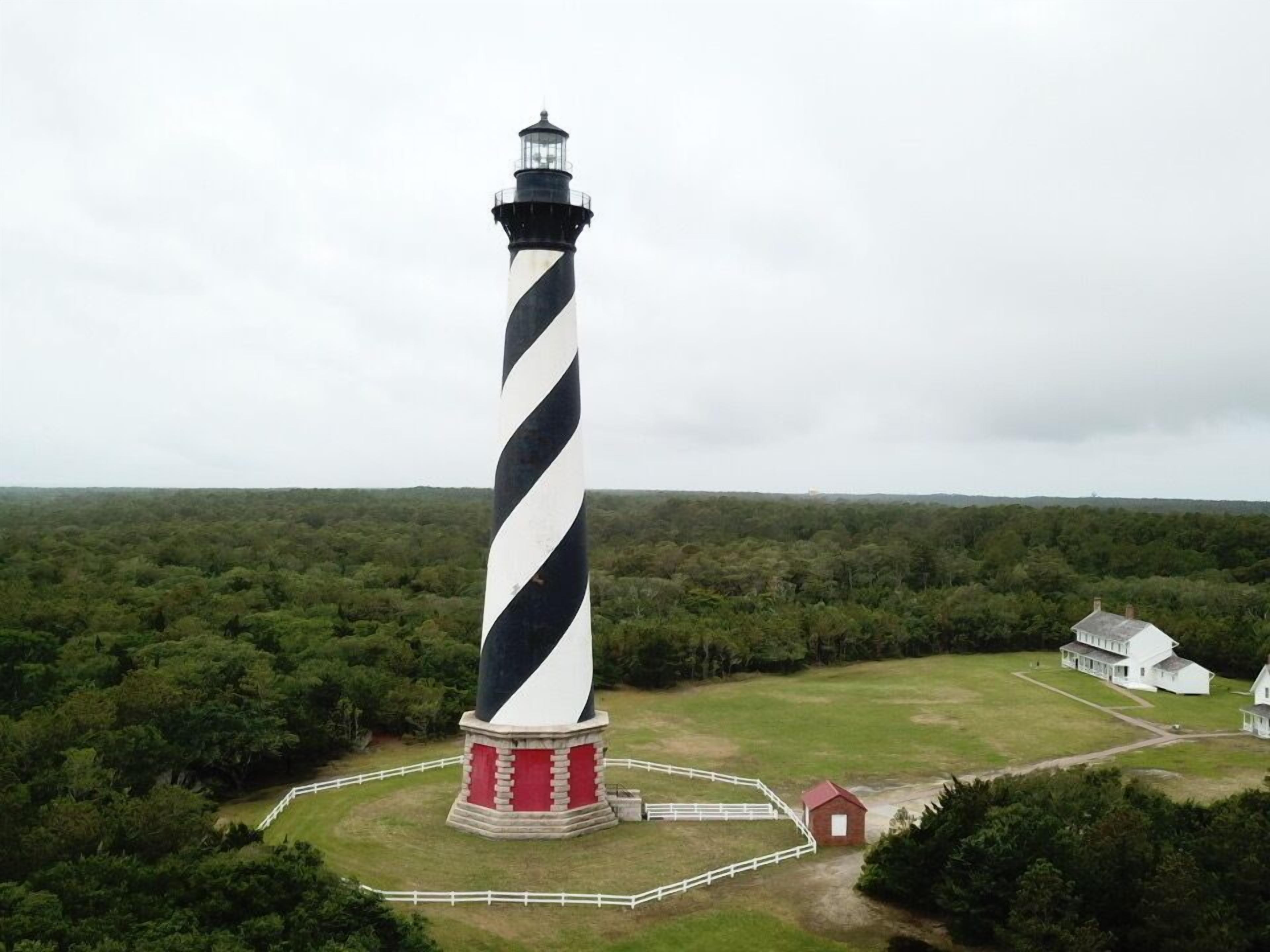 Um farol com design em espiral, cercado por uma grade e um pequeno edifício.