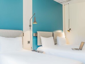 Quarto de hotel moderno com uma cama, um laptop e um abajur.