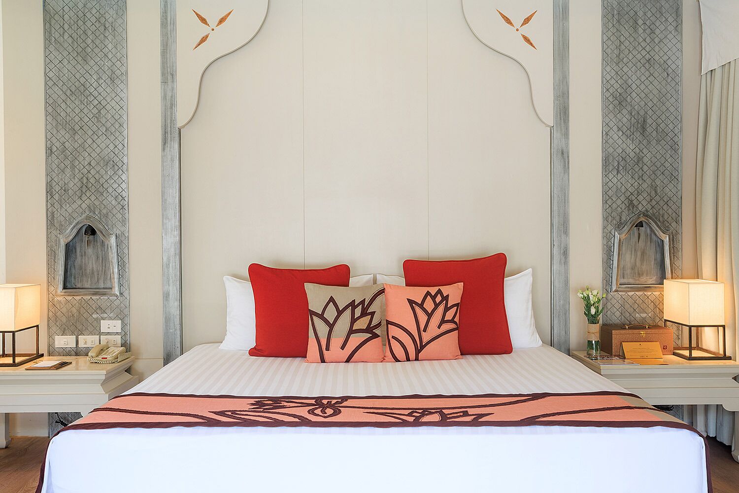 Quarto de hotel com uma cama grande, duas mesas de cabeceira, cabeceira com design decorativo e um espelho na parede.