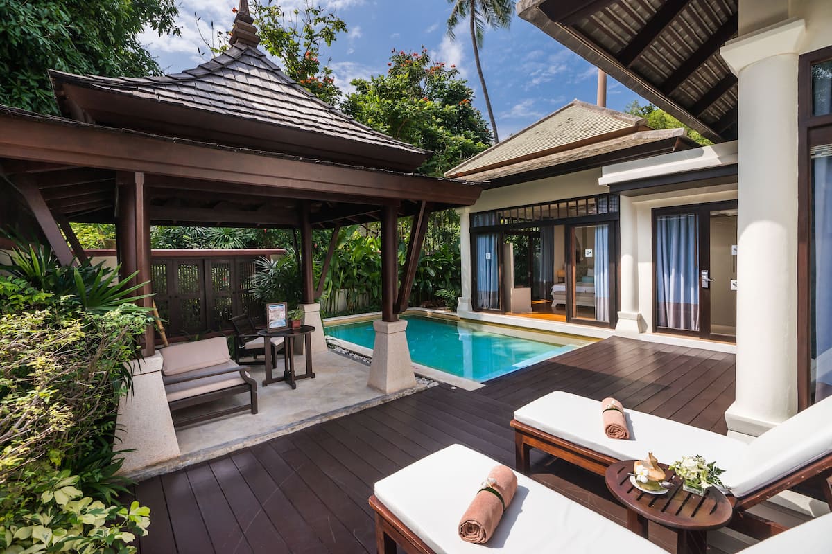 Uma área na piscina com espreguiçadeiras, uma pequena mesa com uma toalha e um gazebo.