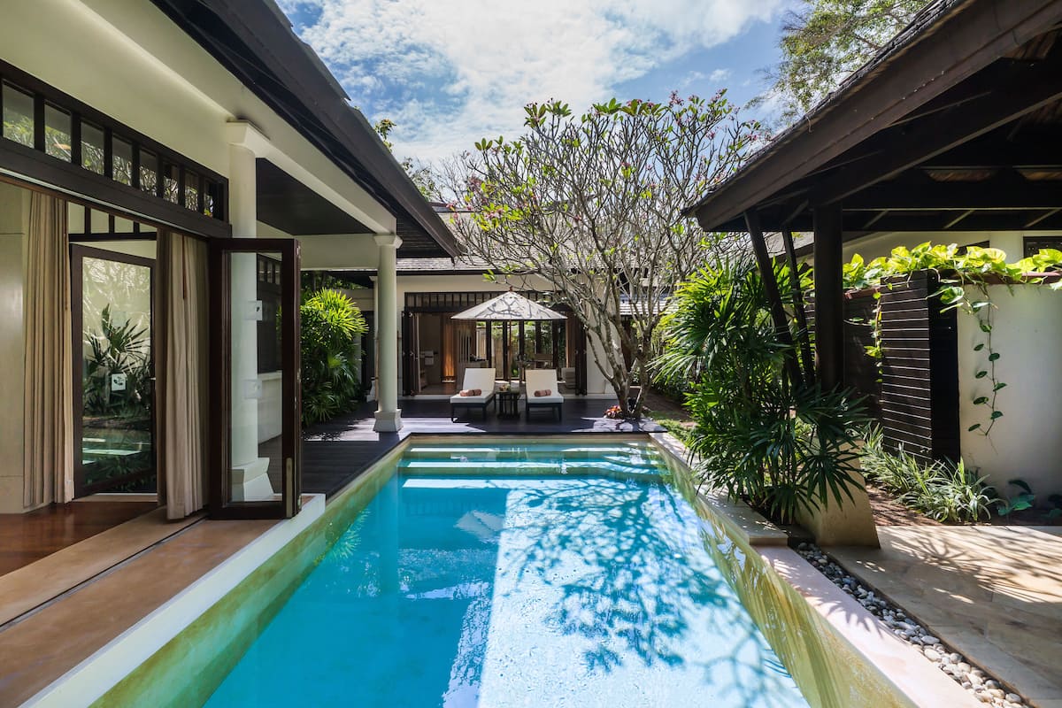 Uma piscina com água azul cristalina, rodeada por um jardim com diversas plantas e um gazebo.