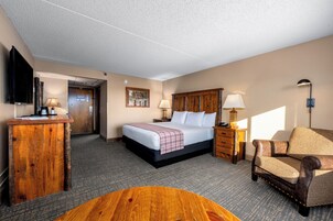 Quarto de hotel com cama, escrivaninha, cadeira, abajur e televisão.