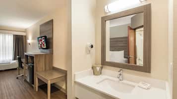 Casa de banho de hotel com lavatório, espelho e televisão na parede.