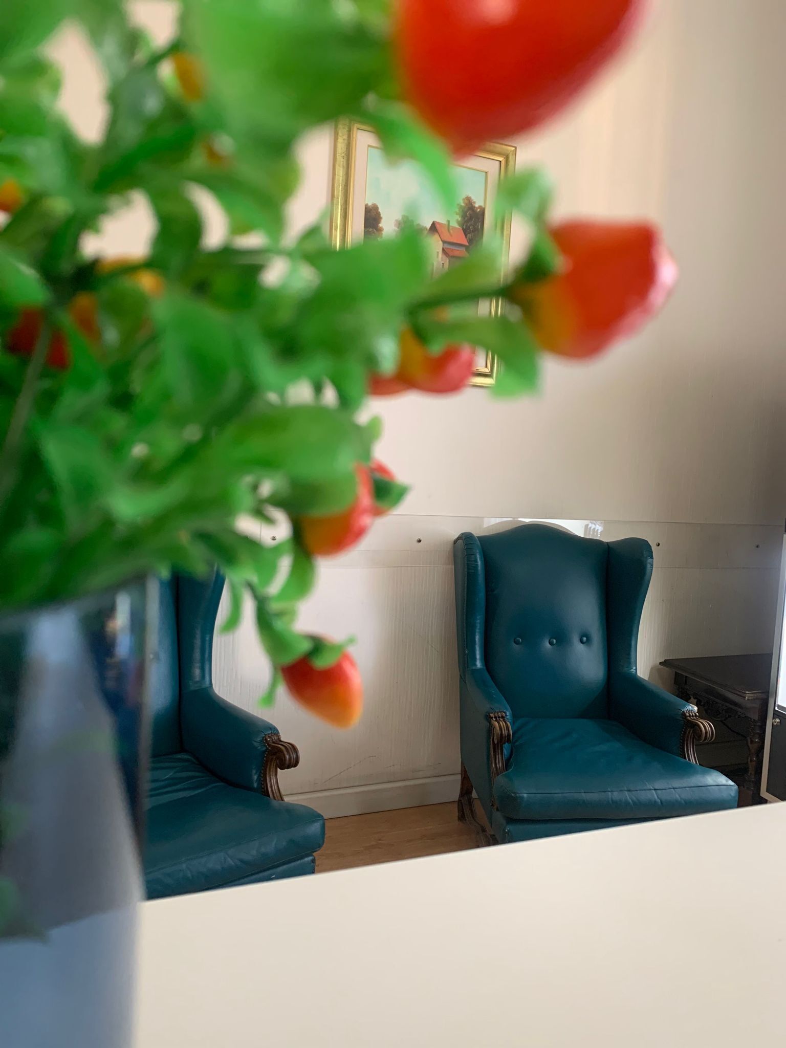 Quarto com duas poltronas azuis, uma mesa branca e um vaso com flores vermelhas e amarelas.