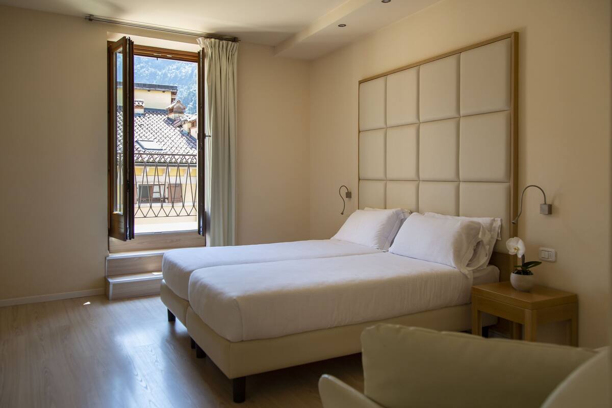 Quarto com uma cama grande, mesa de cabeceira com abajur e vista para uma varanda.