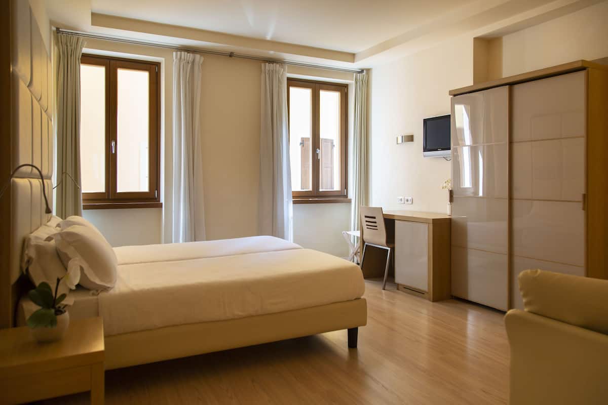 Quarto de hotel com cama, escrivaninha, televisão e guarda-roupa.