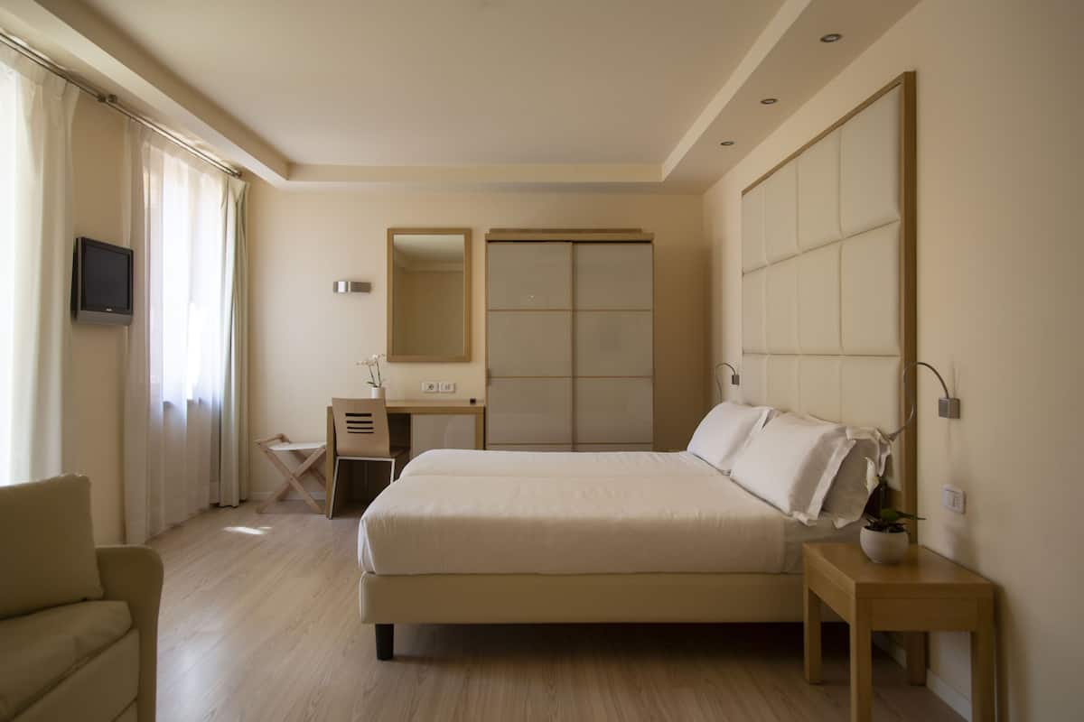 Quarto com cama, mesa de cabeceira, cadeira, escrivaninha, espelho, guarda-roupa e televisão.