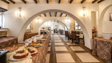 Uma longa área de jantar com um arco central, mesas servidas com comida e vista para a sala de jantar.