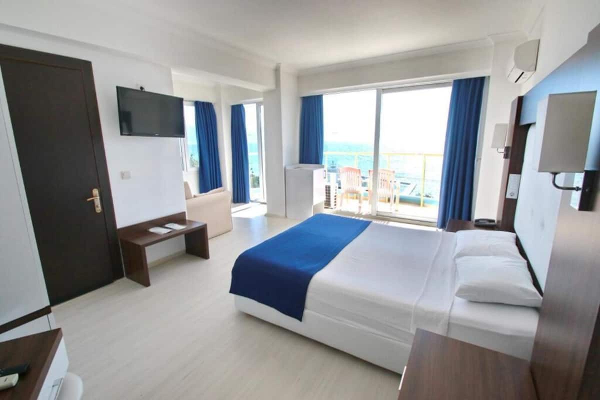 Quarto de hotel com cama, escrivaninha, televisão e varanda vista para o mar.