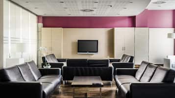 Uma sala de estar moderna com televisão de tela plana na parede, sofás de couro, uma mesa de centro e uma janela grande que proporciona iluminação natural.