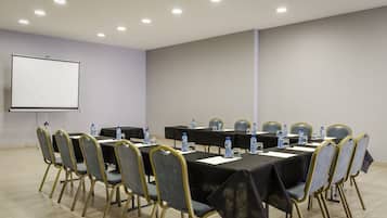 Sala de conferência com uma mesa comprida, cadeiras, garrafas de água e uma tela de projetor.