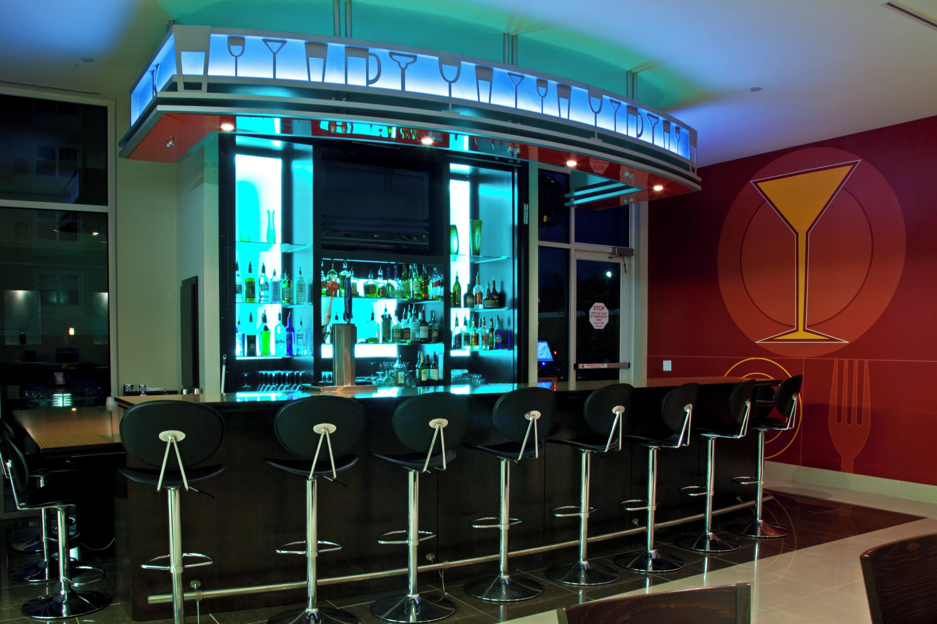 Uma área de bar com balcão curvo, vários bancos e uma variedade de garrafas.