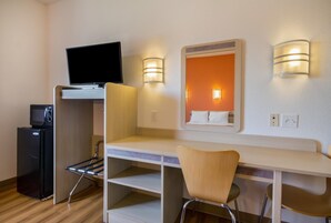Quarto de hotel com uma escrivaninha, uma cadeira, uma televisão e um pequeno frigorífico.