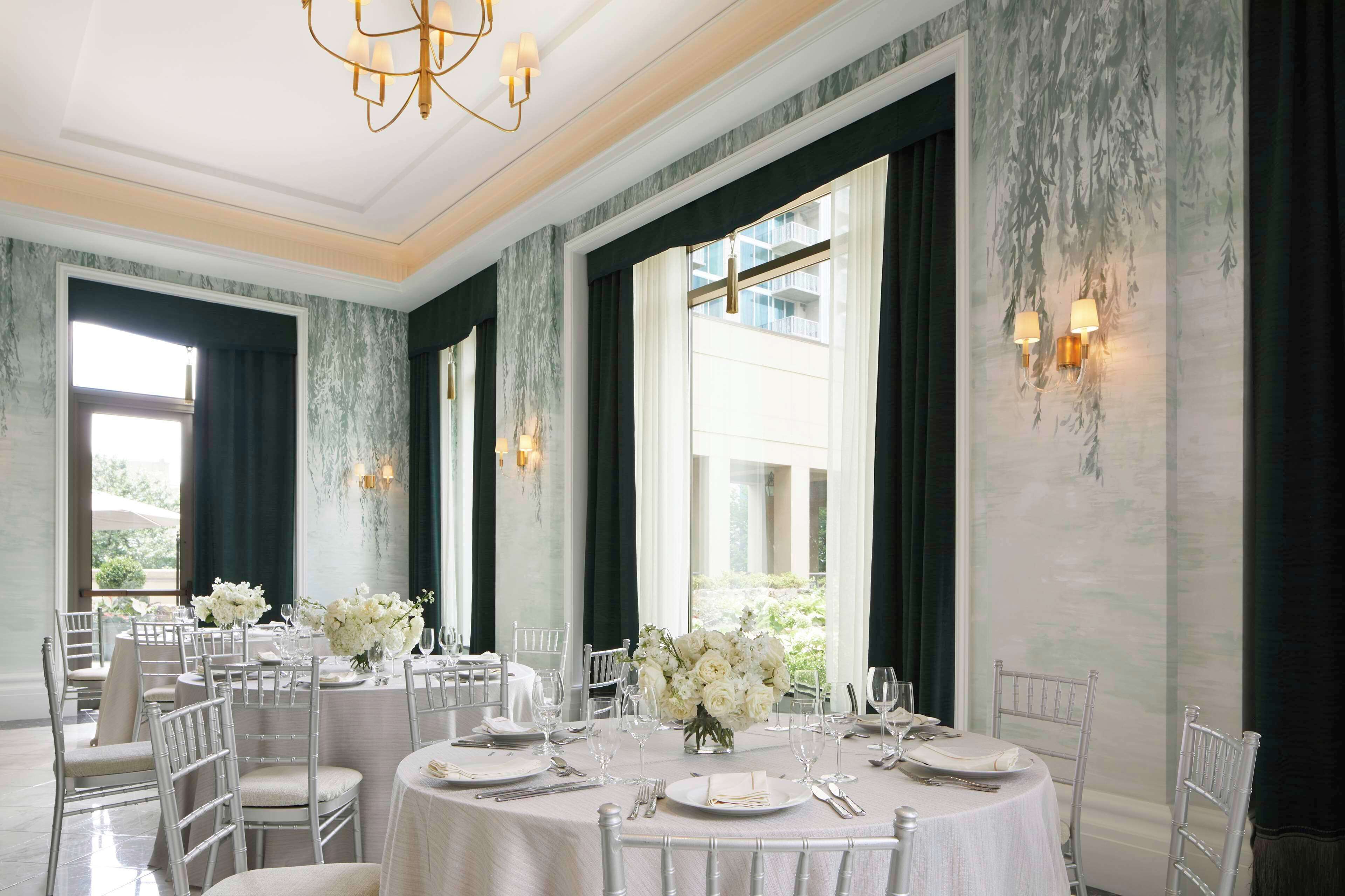 Uma sala de jantar formal com mesas redondas, toalhas brancas e cadeiras de prata.