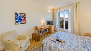 Quarto de hotel com cama, escrivaninha com televisão, cadeira e um quadro na parede.