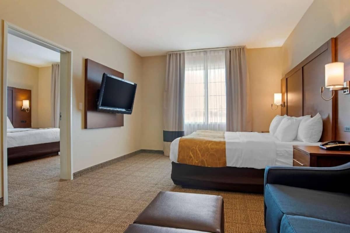Quarto de hotel com cama, televisão, escrivaninha e cadeira.