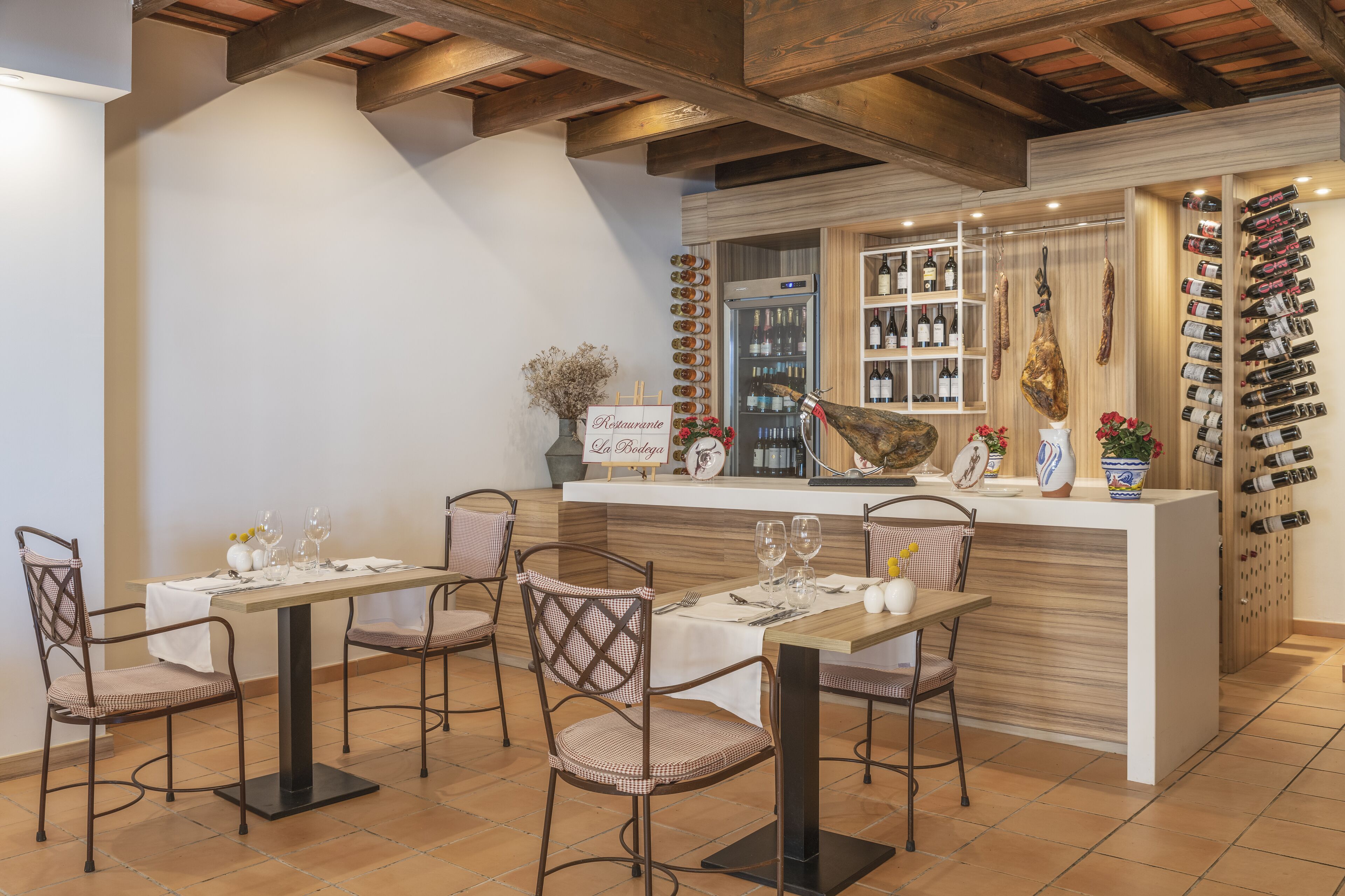Restaurante com teto de madeira, espaço para exibição de vinhos e balcão com garrafas.