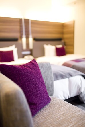Quarto de hotel com cama, sofá e mesa de cabeceira com abajur.