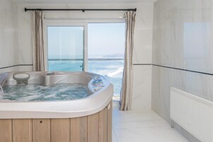 Uma casa de banho moderna com hidromassagem, janelas grandes e vista para o oceano.