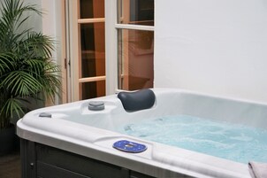 Uma banheira de hidromassagem com painel de controle, um vaso de planta e uma janela com persianas.