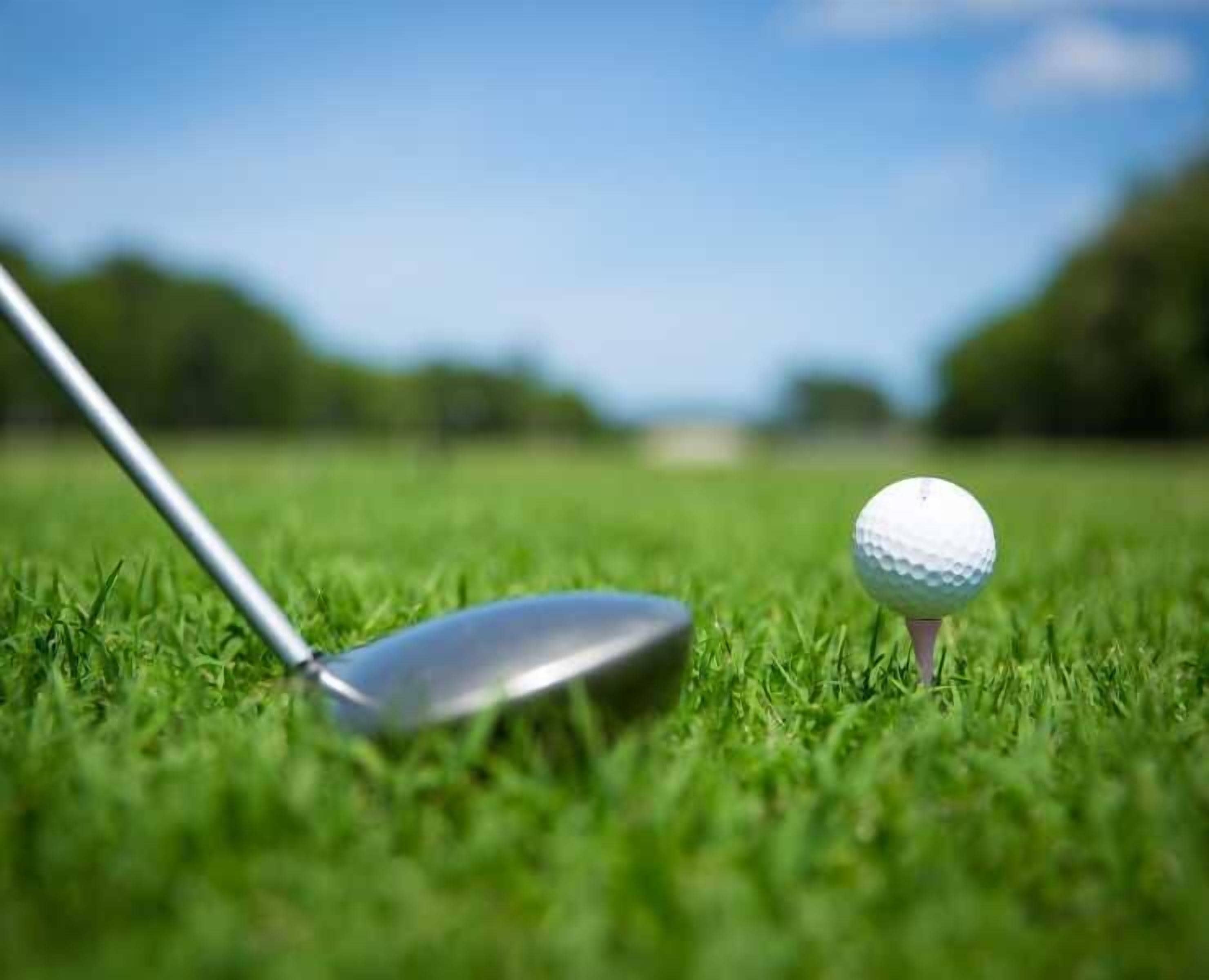 Uma bola de golfe em um tee num campo relvado, com um taco de golfe por perto.