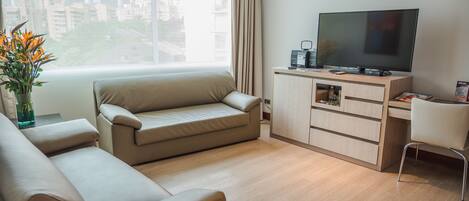 Uma sala de estar moderna com sofá, televisão, aparador e vista para a paisagem urbana através de uma grande janela.