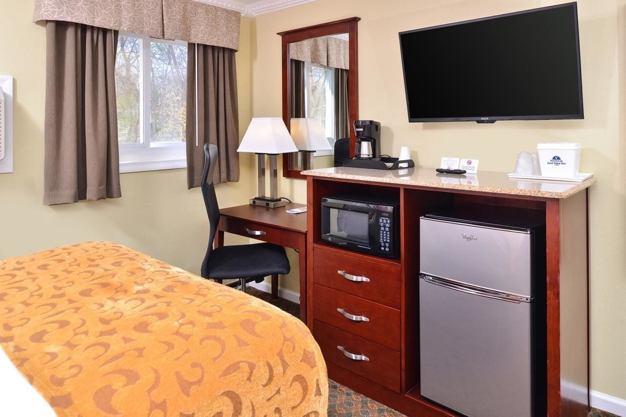 Quarto de hotel com cama, escrivaninha com computador, micro-ondas, frigorífico, máquina de café e televisão de ecrã plano.