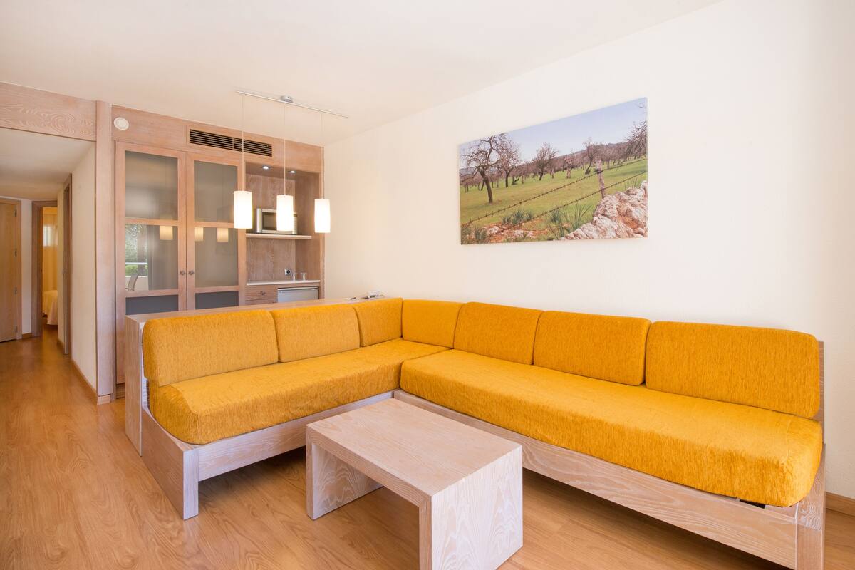 Uma sala de estar moderna com um sofá modular amarelo, uma mesa de centro de madeira e uma grande janela com vista para um vinhedo.