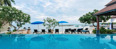 Uma piscina com águas cristalinas, cadeiras de descanso e guarda-sóis, com vista para uma praia com cadeiras de descanso e guarda-sóis.
