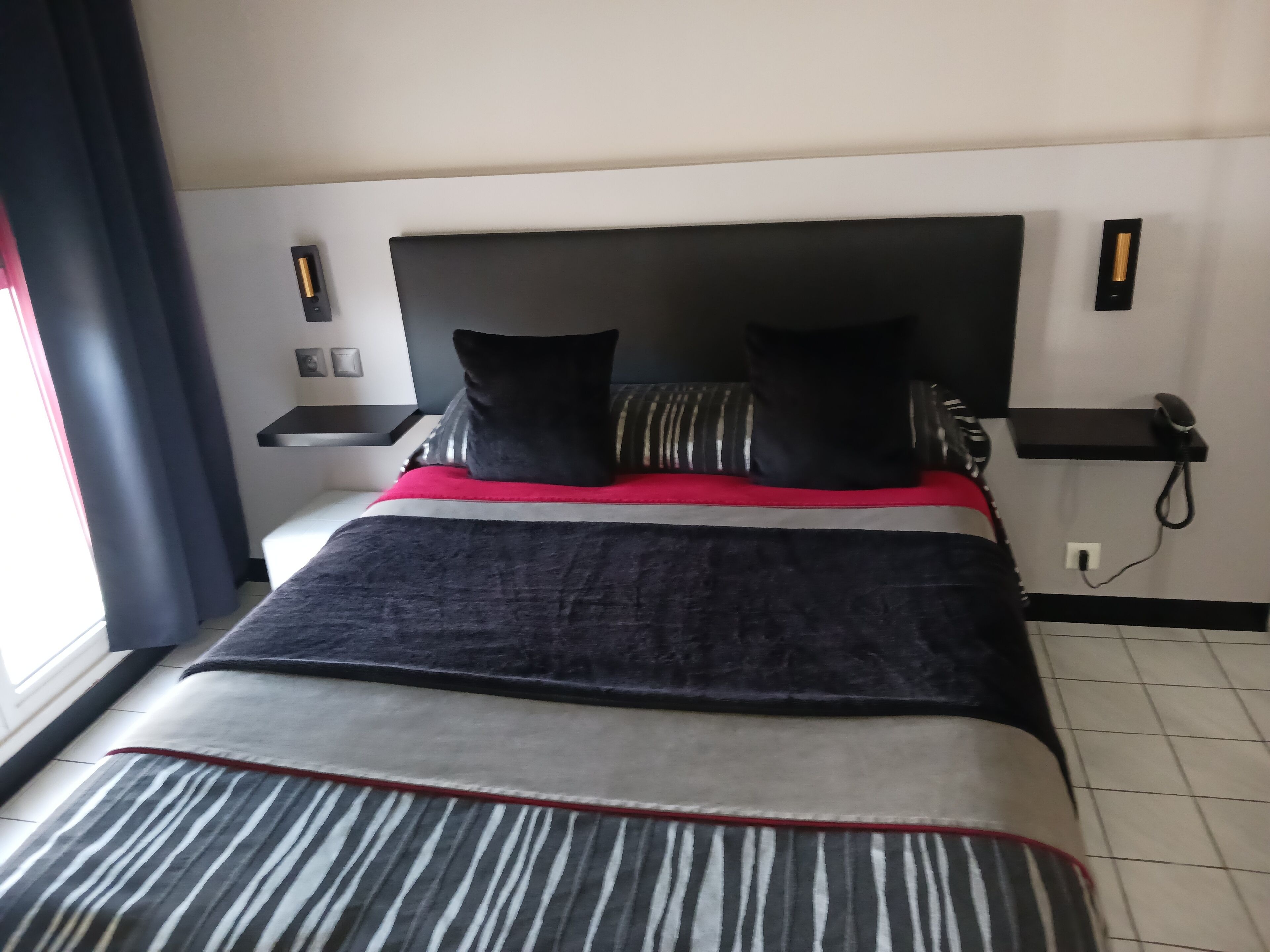 Cama bem arrumada com colcha listrada, dois travesseiros e um detalhe em vermelho.