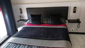 Cama bem arrumada com colcha listrada, dois travesseiros e um detalhe em vermelho.