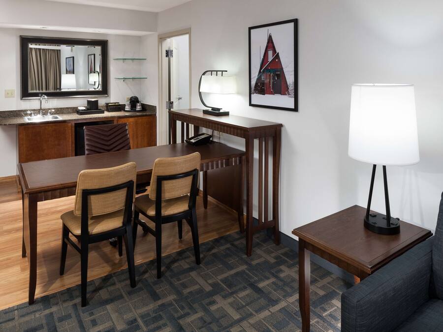 Quarto de hotel com área de jantar, uma mesa pequena com abajur, sofá e quadro na parede.