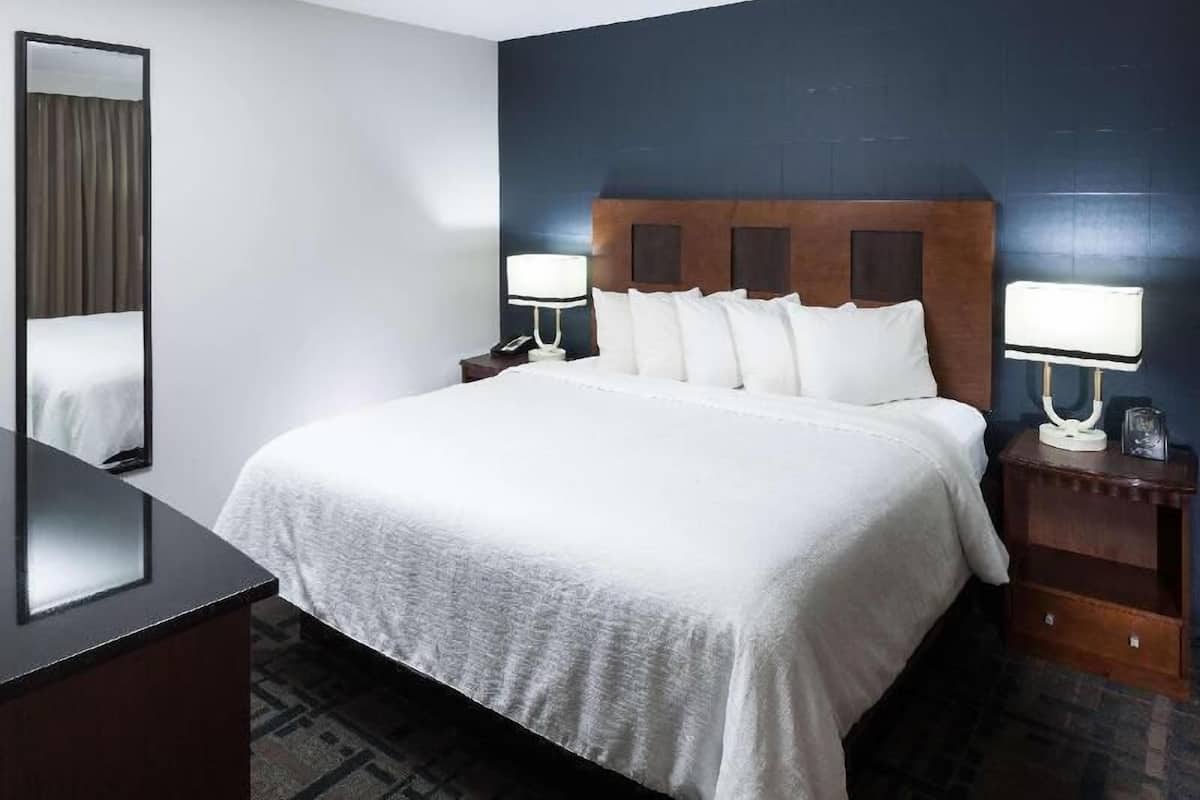 Quarto de hotel com cama grande, mesa de cabeceira, espelho e cómoda.
