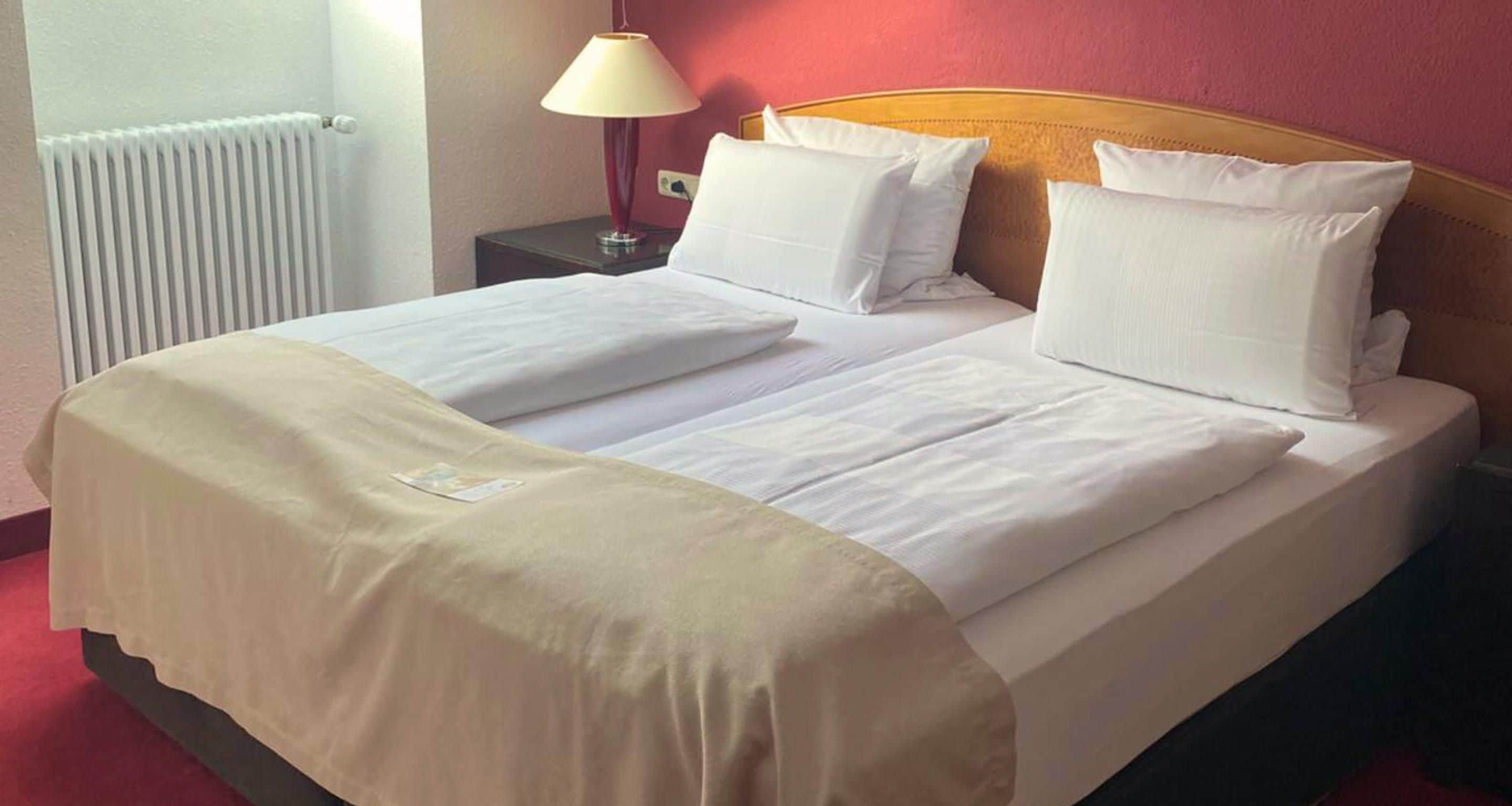 Uma cama de casal com lençóis brancos, cabeceira de madeira e mesa de cabeceira com abajur.