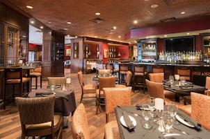 Restaurante com piso de madeira, cadeiras de vime e mesas postas para refeições.