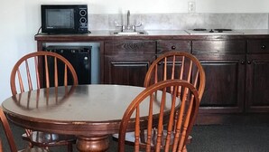 Uma área de refeições com uma mesa de madeira redonda e quatro cadeiras, um micro-ondas, uma pia e um fogão ao fundo.